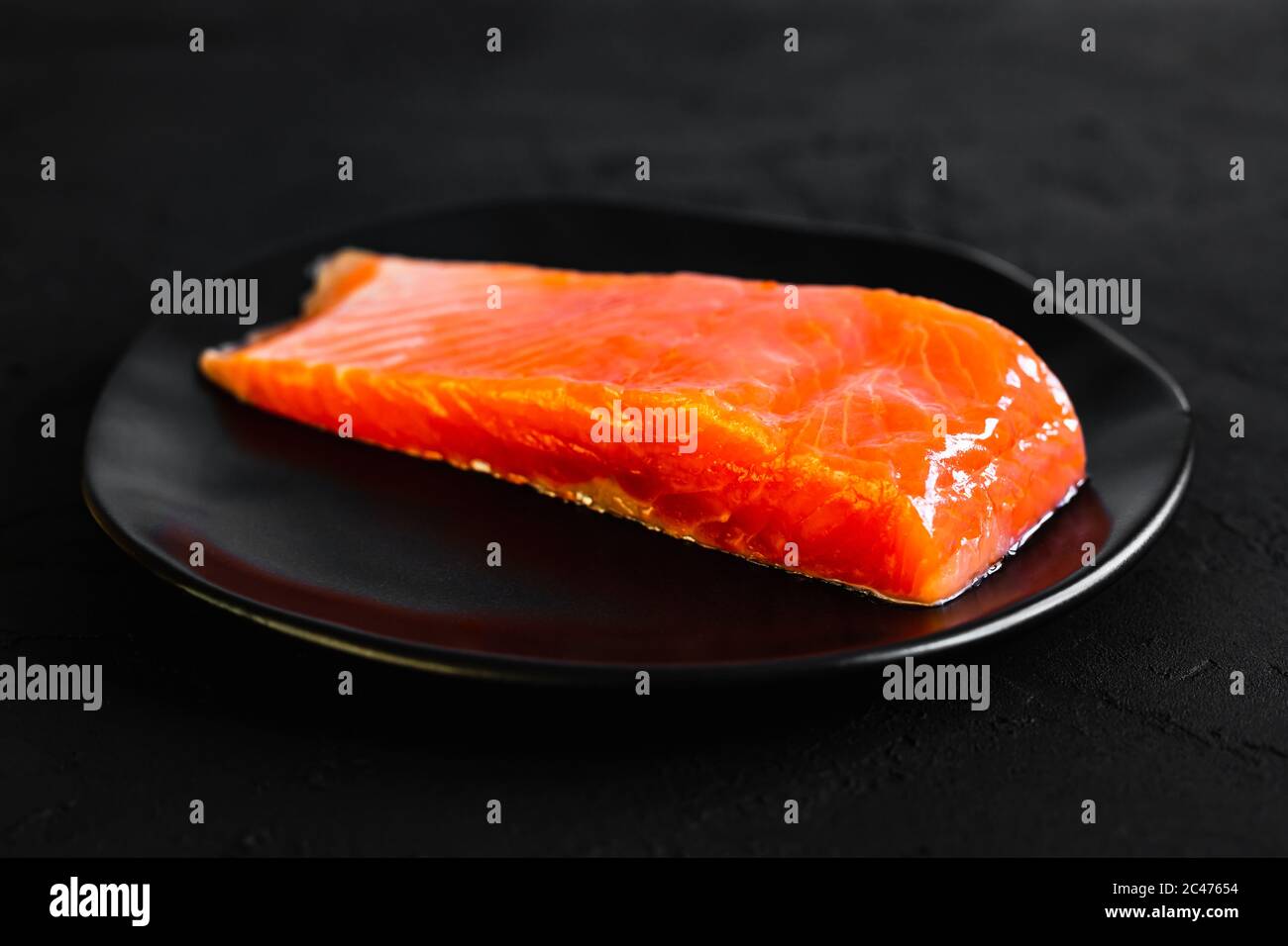 Salted red fish on a black plate on black background, a close-up photo ...