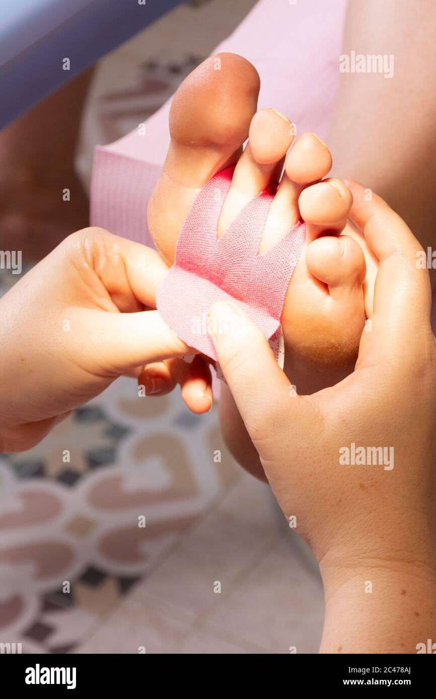 The hands of an unrecognizable podiatrist woman placing a pink kinesio ...