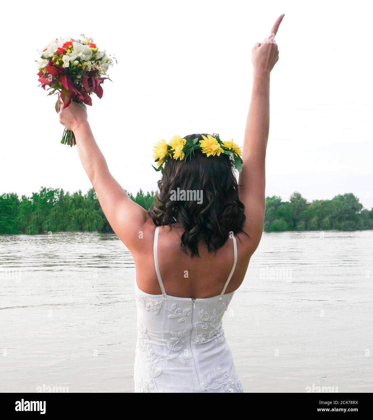 Bride by the river with a flower wreath on her head ready to throw a ...