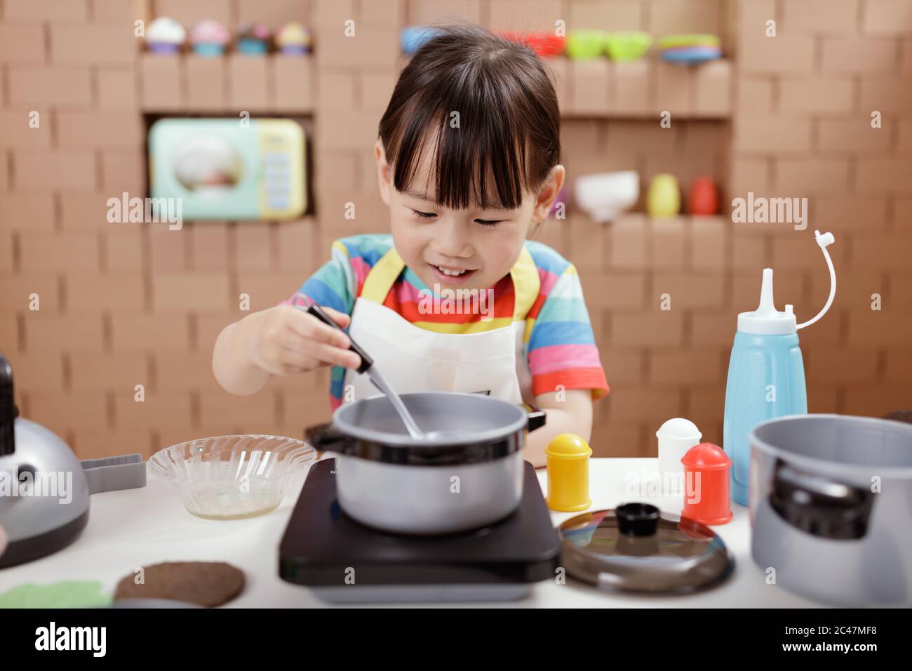 toddler girl pretend play food preparing role against cardboard blocks ...