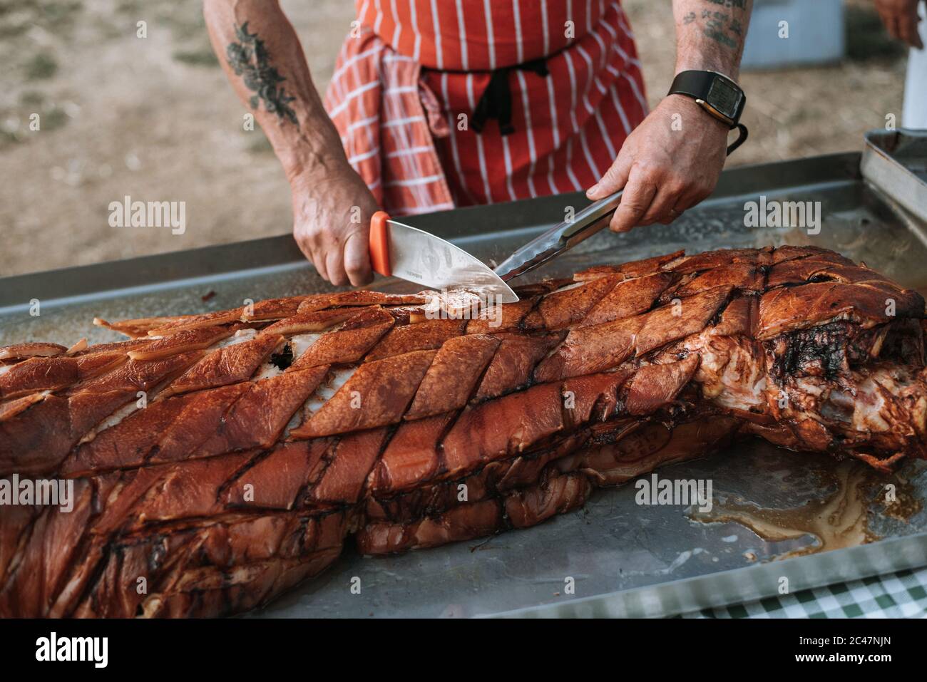 Man cutting a piece from a delicious roasted, crispy skinned whole pig ...
