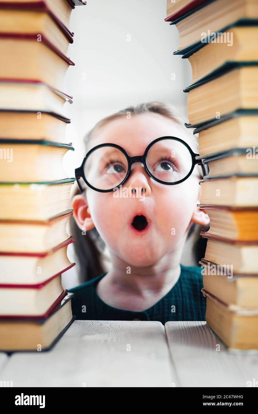 Shocked little blonde kid girl 4-6 years old in library among many ...