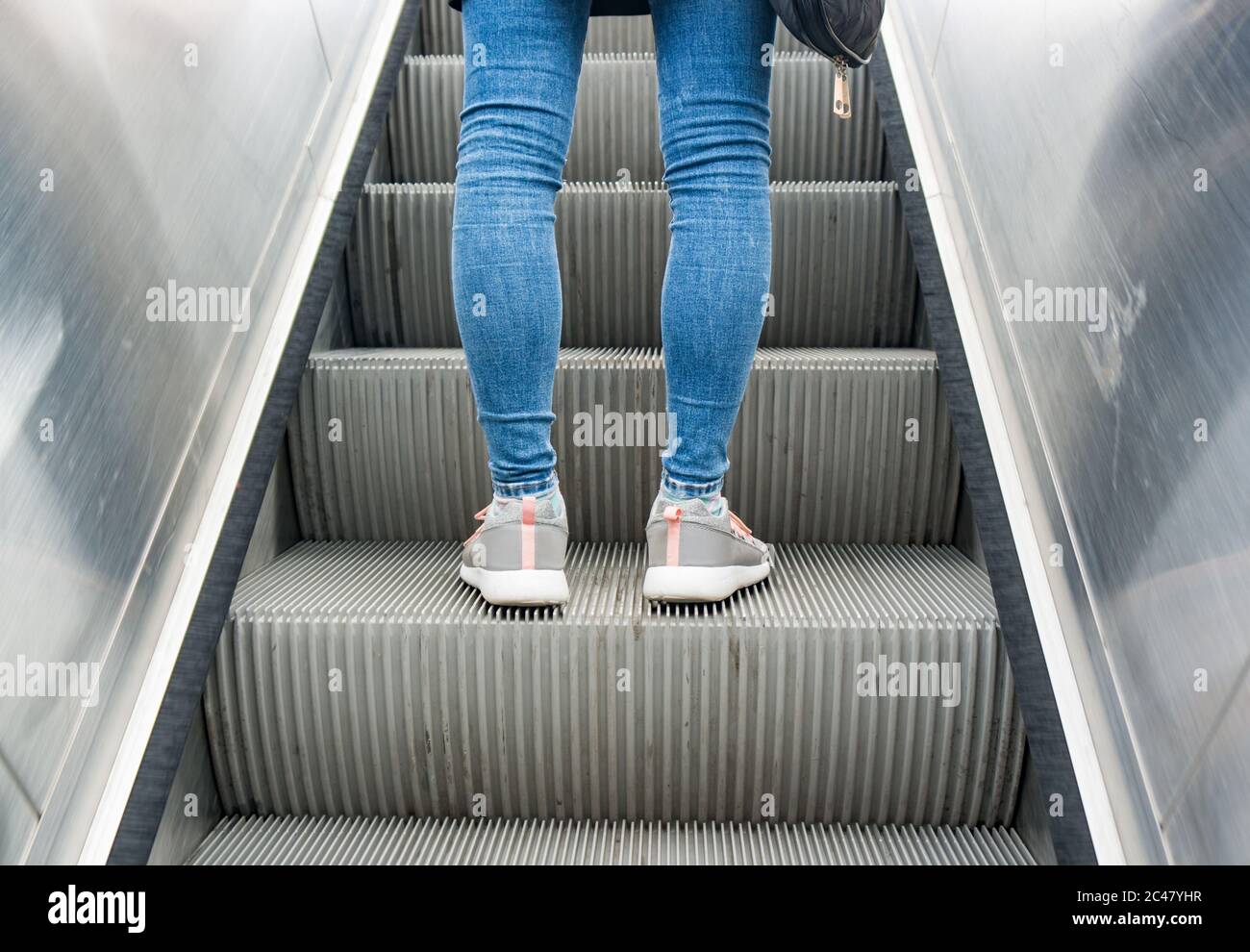 Closeup shot of female legs in jeans and sport shoes on an escalator ...