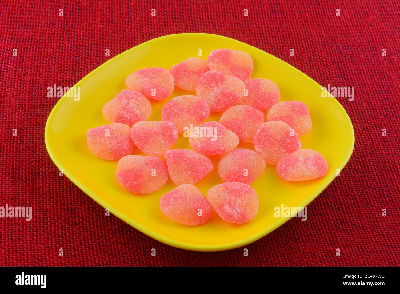 Closeup of sweet peach gummy candy pieces on yellow snack plate on red ...