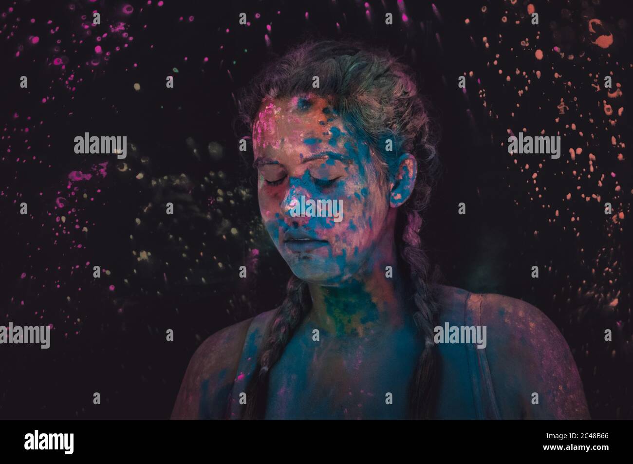 Colorful paint splashed on the face of a young female with a black ...