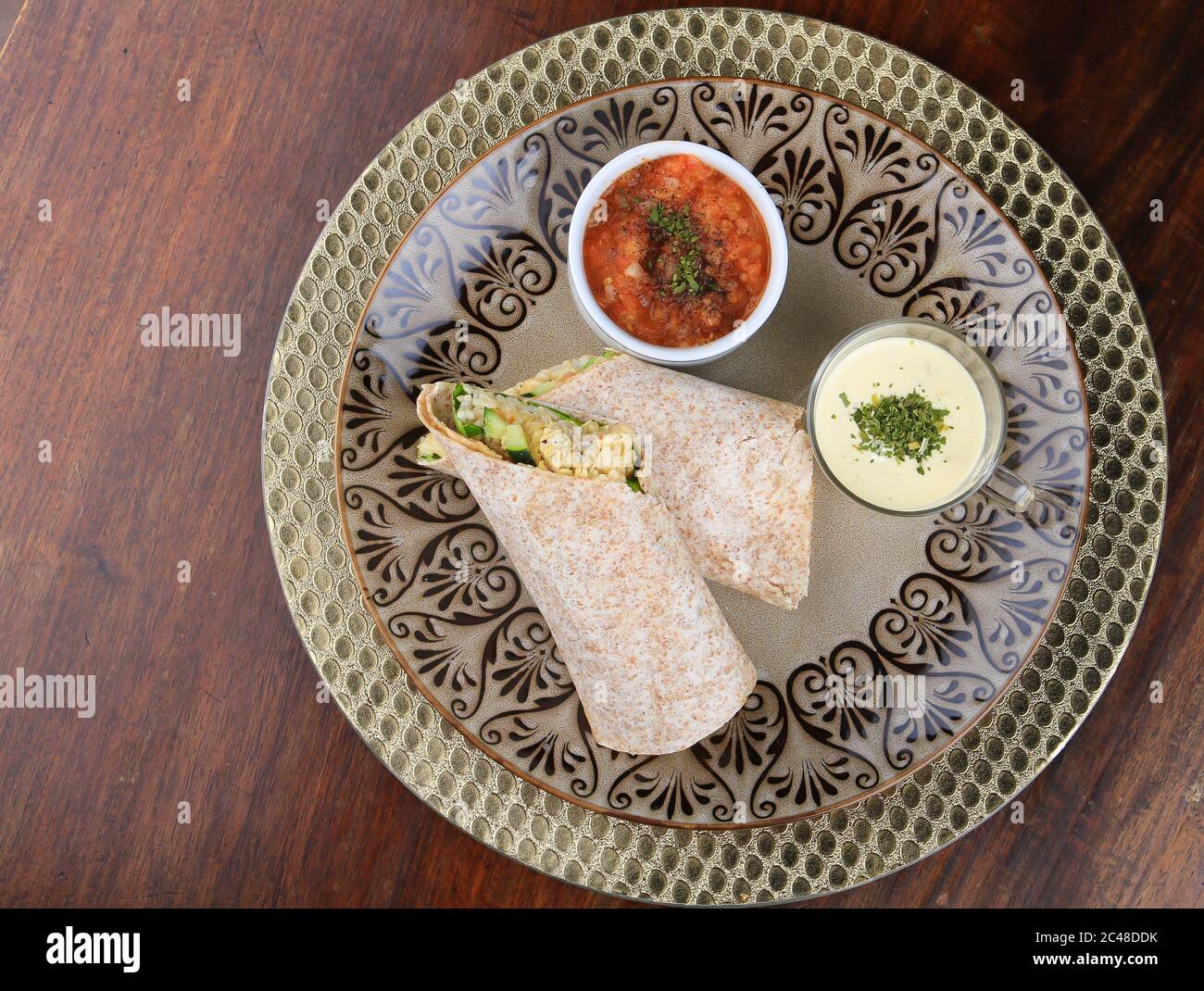 Burrito cut in half and some sauces served on a plate with patterns ...