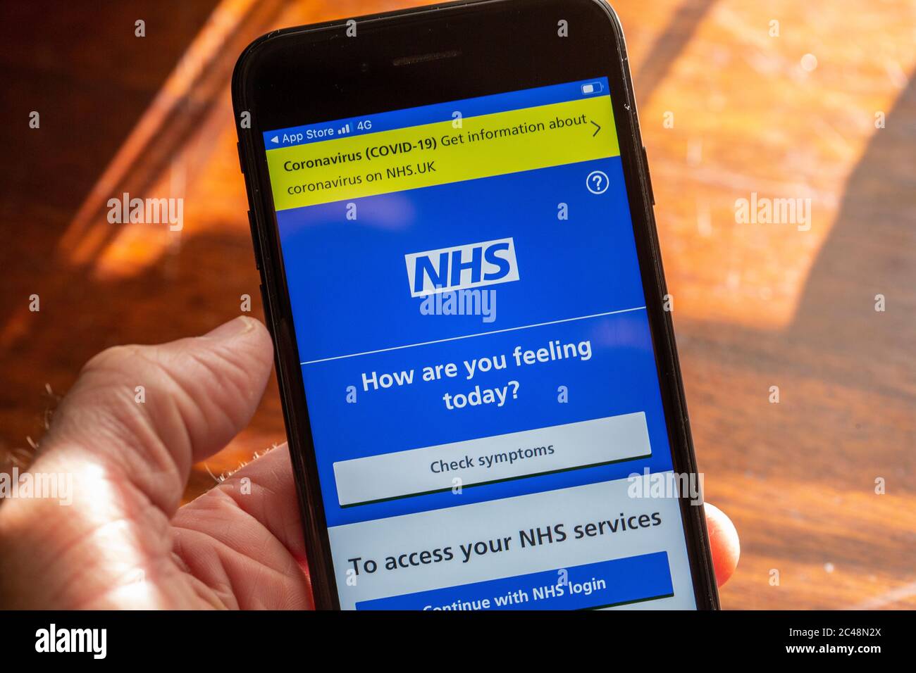 A hand holding a black mobile phone showing the NHS App. Photo by Sam ...