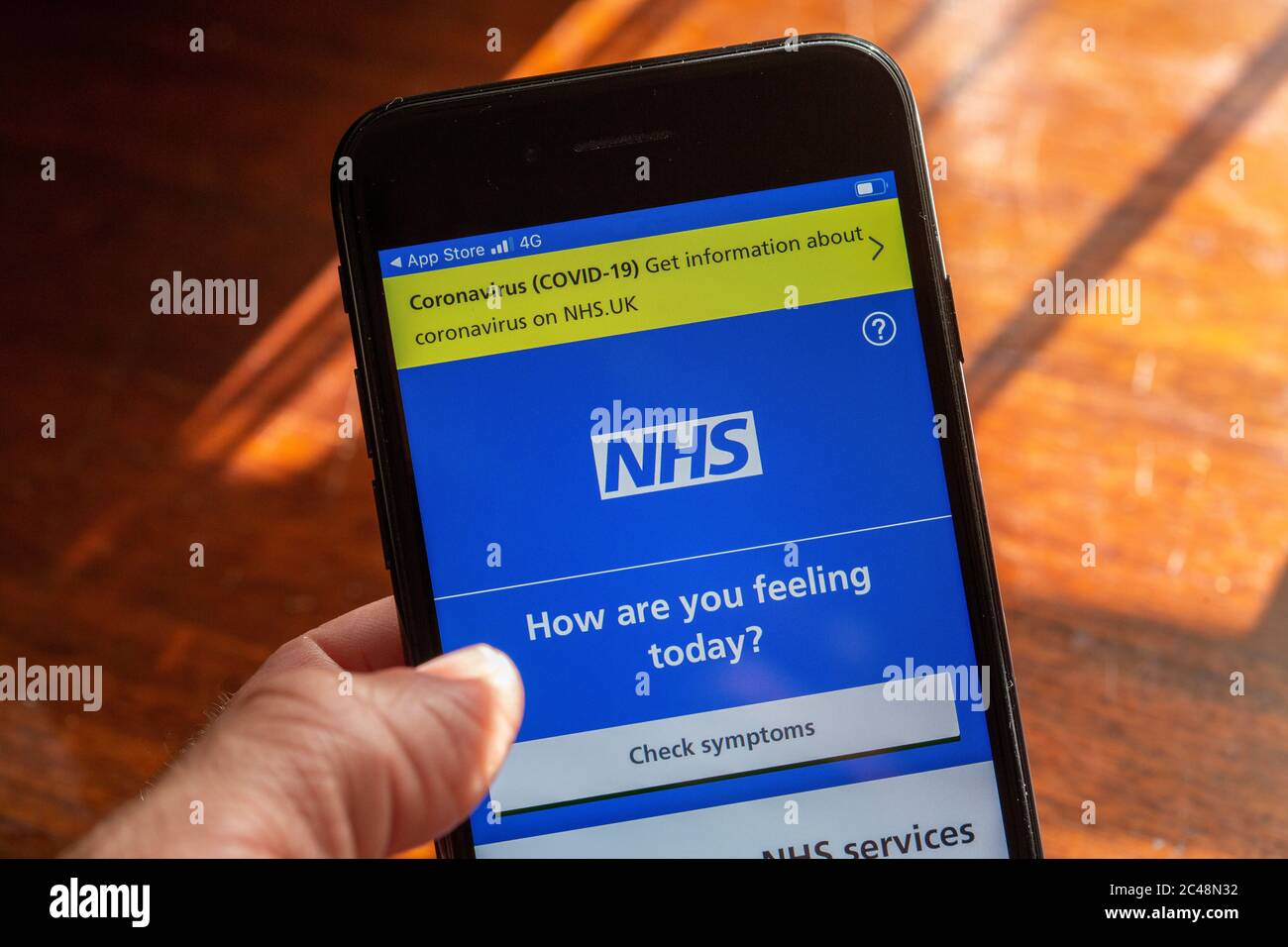 A hand holding a black mobile phone showing the NHS App. Photo by Sam ...