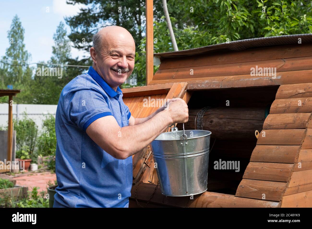 Man draw water from the well to water flowers in garden Stock Photo - Alamy