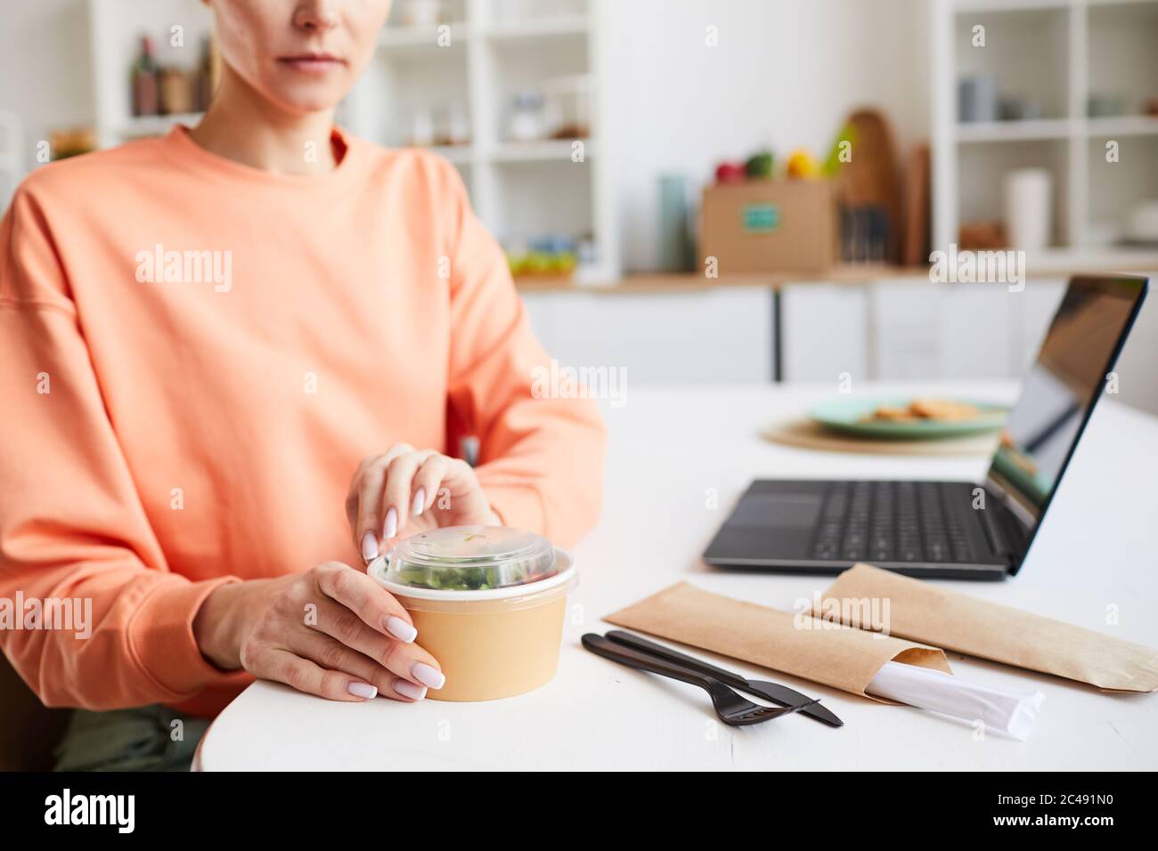 Close-up of woman sitting at the table and opening the box with food ...