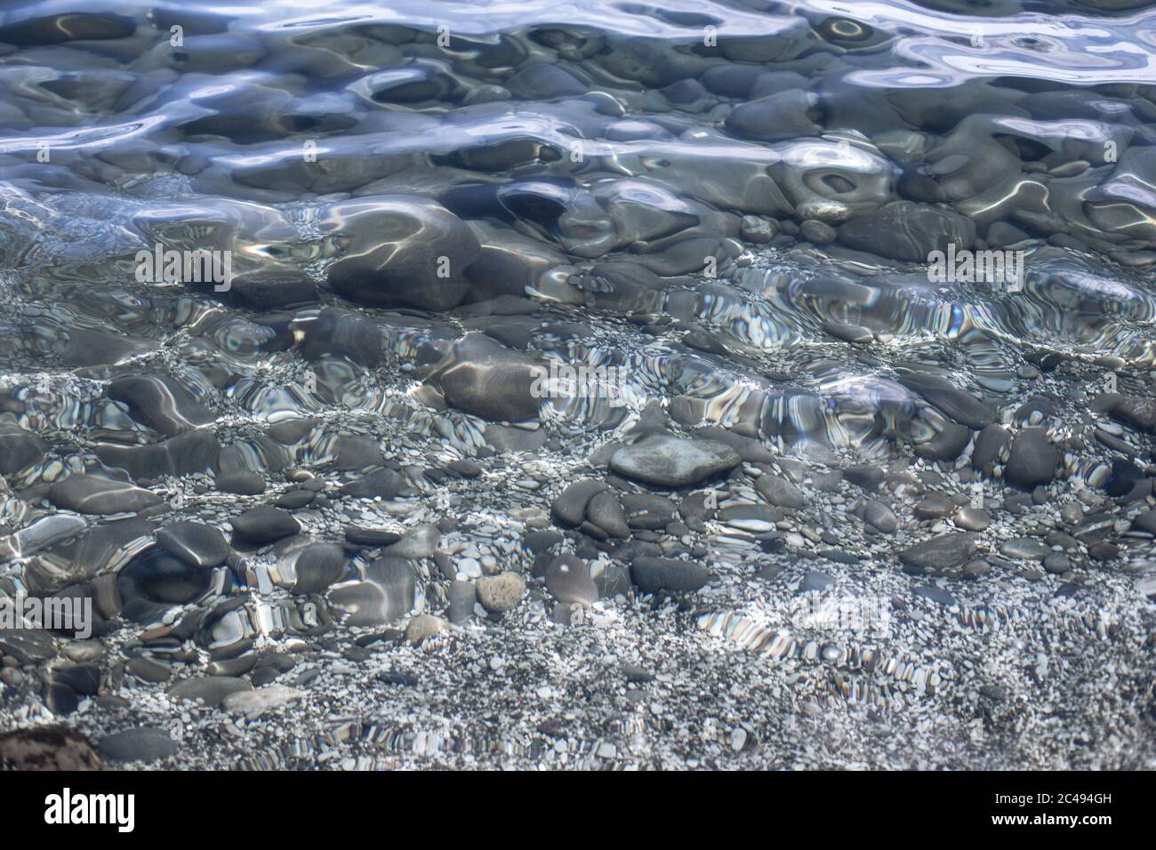 Closeup of transparent clear calm water surface with small grey pebbles ...