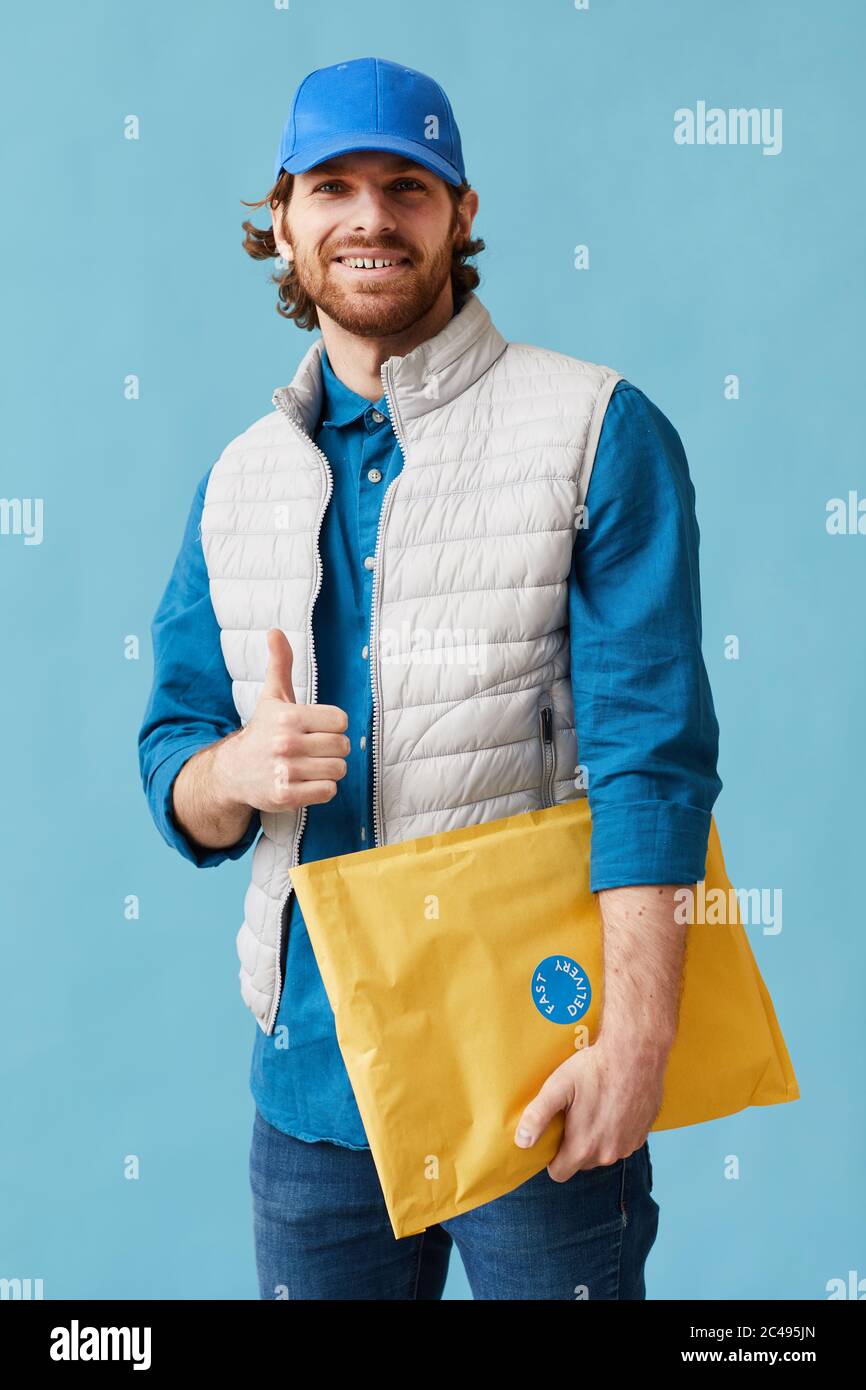 Portrait of smiling postman in uniform holding big parcel and showing ...