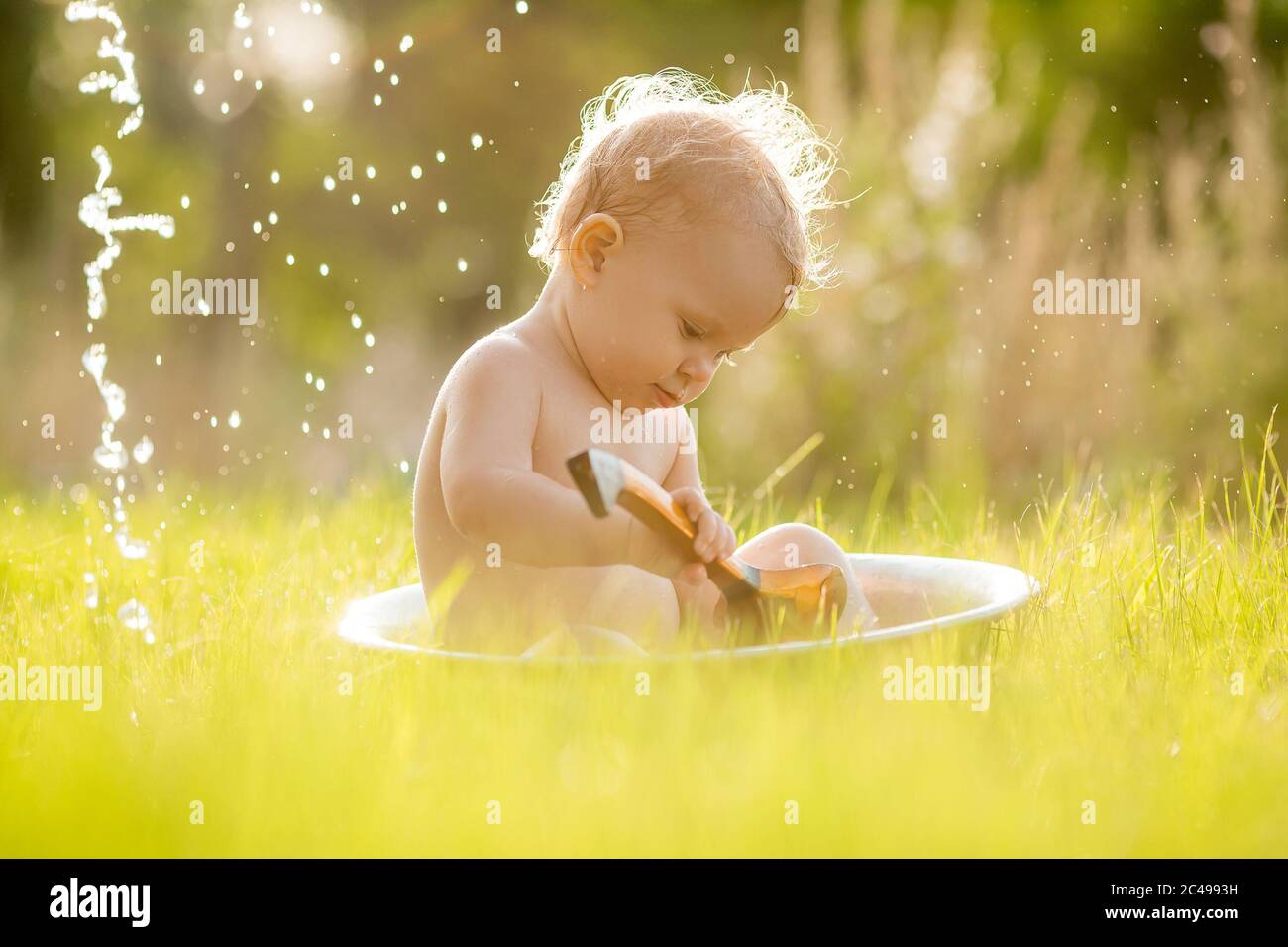 Cute little girl sits in a basin of summer water on the green grass ...