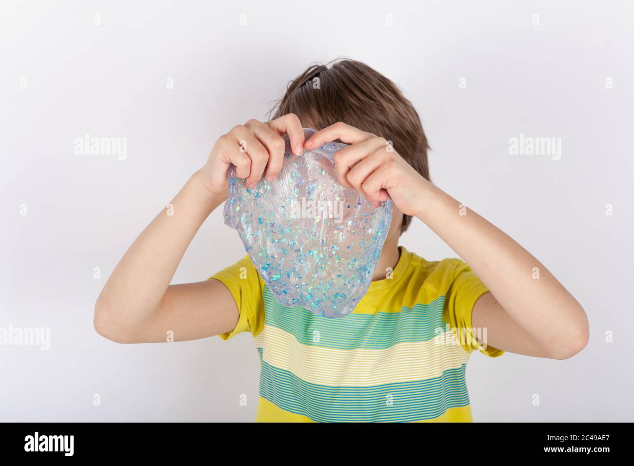 Young boy holding a transparent glitter slime in front of his face ...