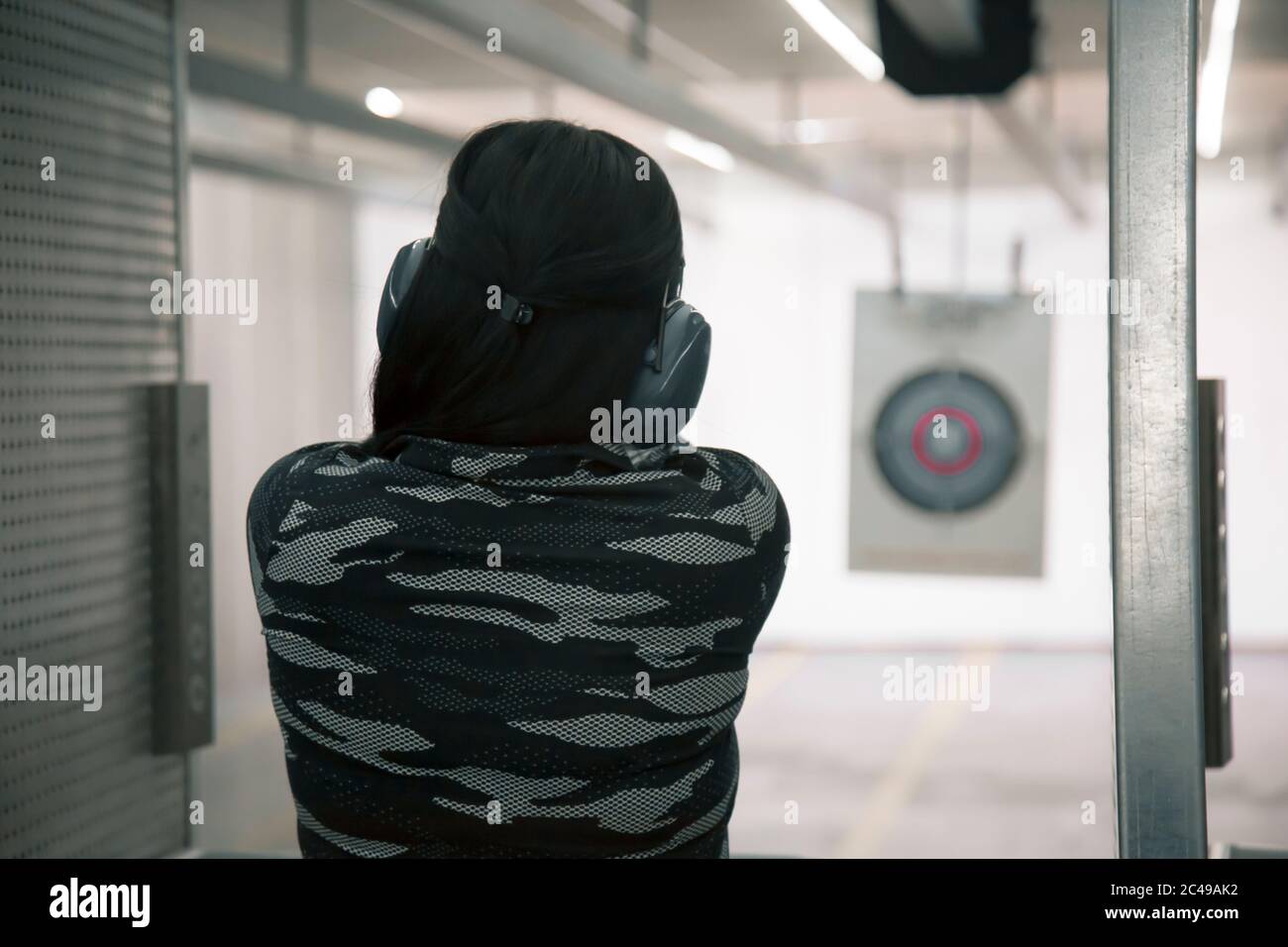 Woman aiming pistol at target in indoor firing range or shooting range ...