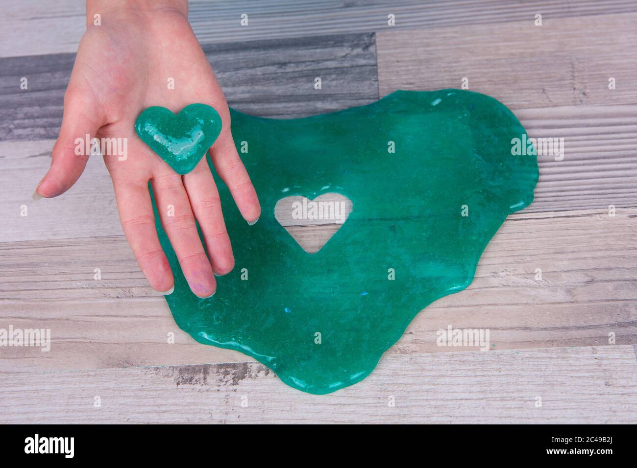 Hand with heart shape green slime in front of a wooden background with ...