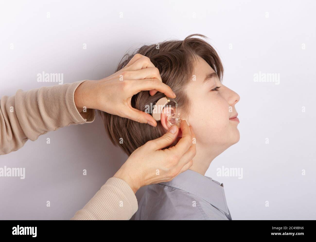Audiologist fitting hearing aid on a smilling young boy's ear Stock ...