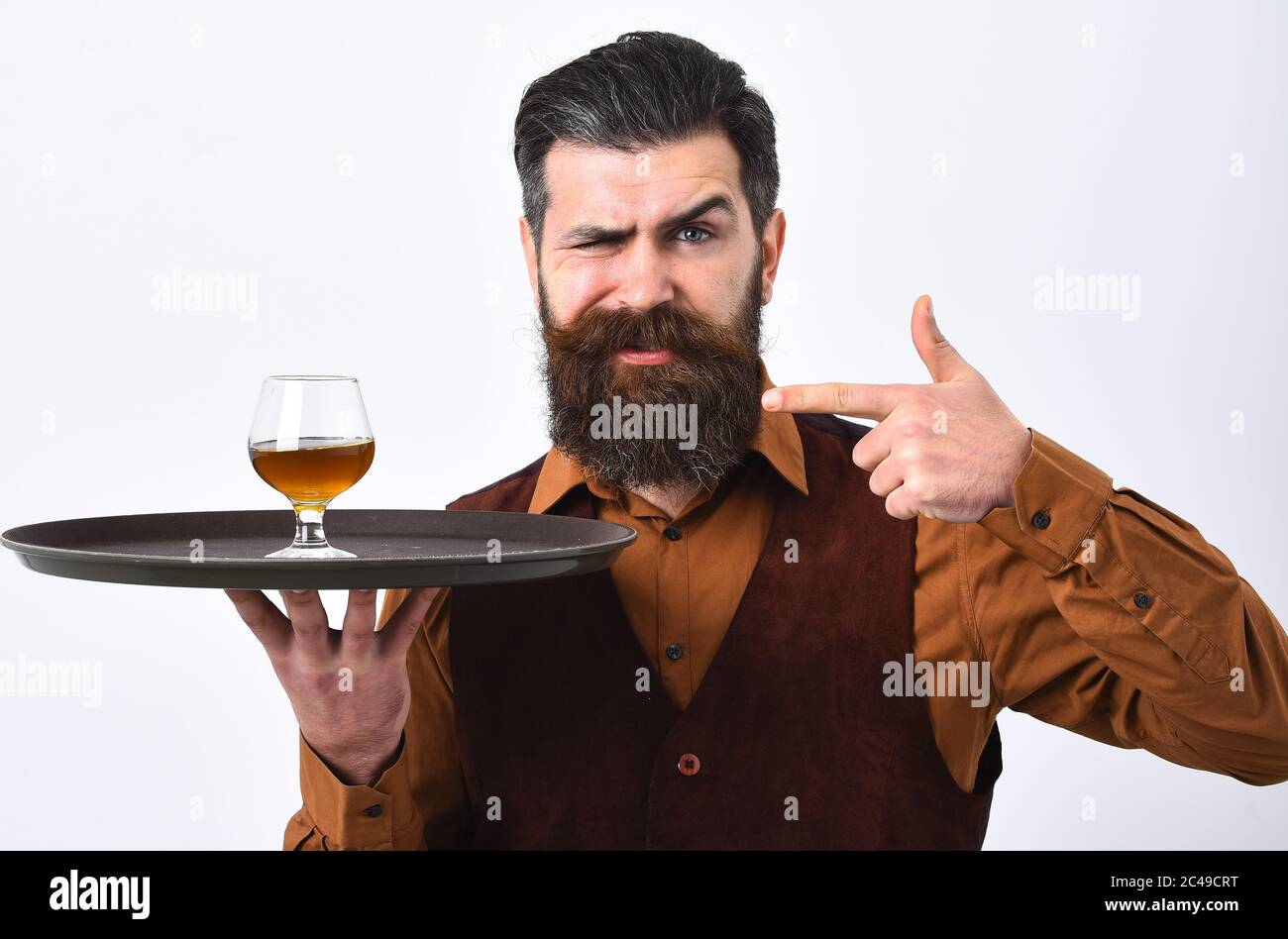 Barman with proud face and in vintage vest serves cognac. Waiter points ...