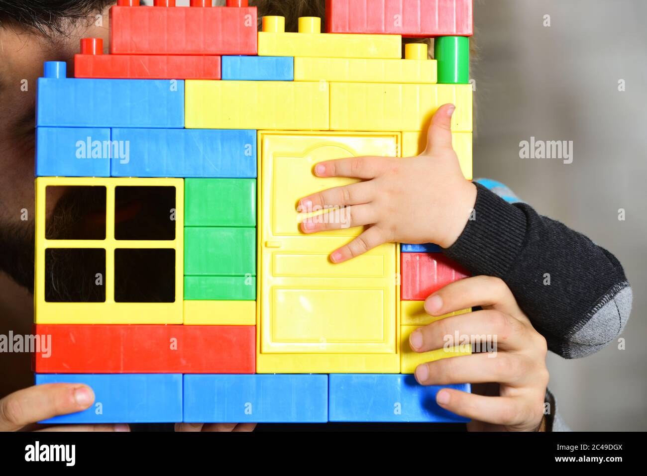 Dad and kid hide behind building wall made of plastic blocks. Guys play ...