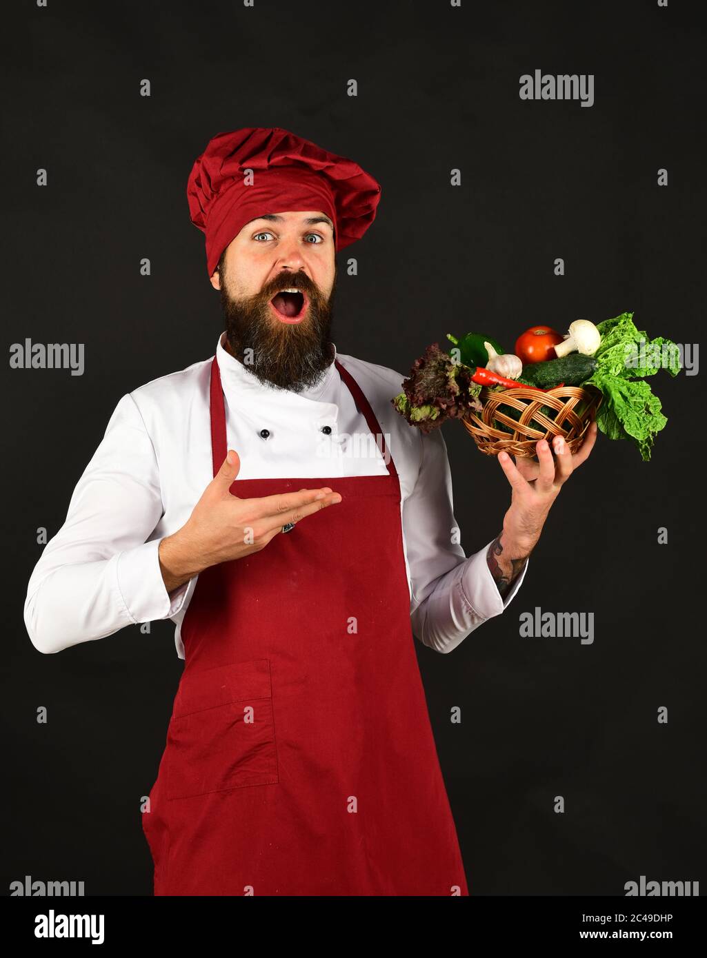 Cook with surprised face in burgundy uniform presents vegetables in ...