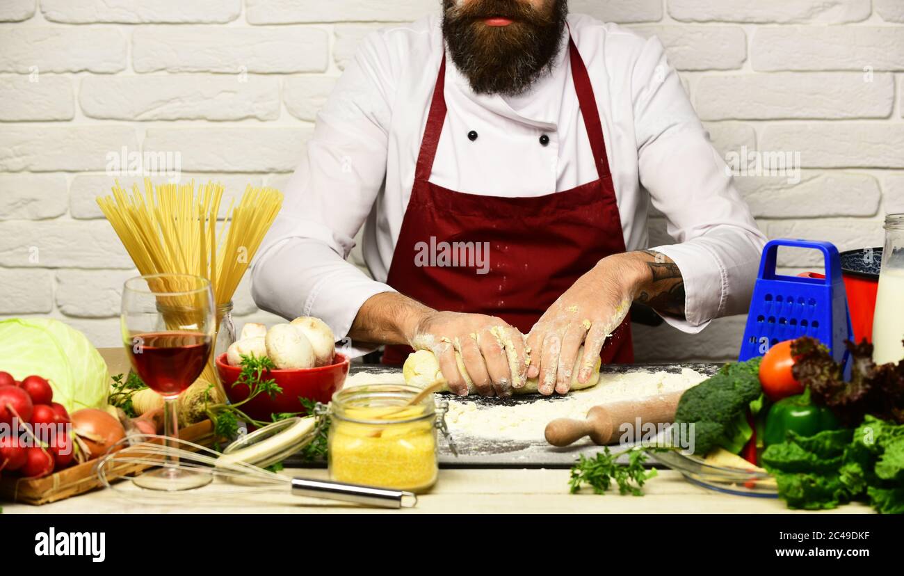 Chef makes dough. Man with beard kneads dough on white brick wall ...