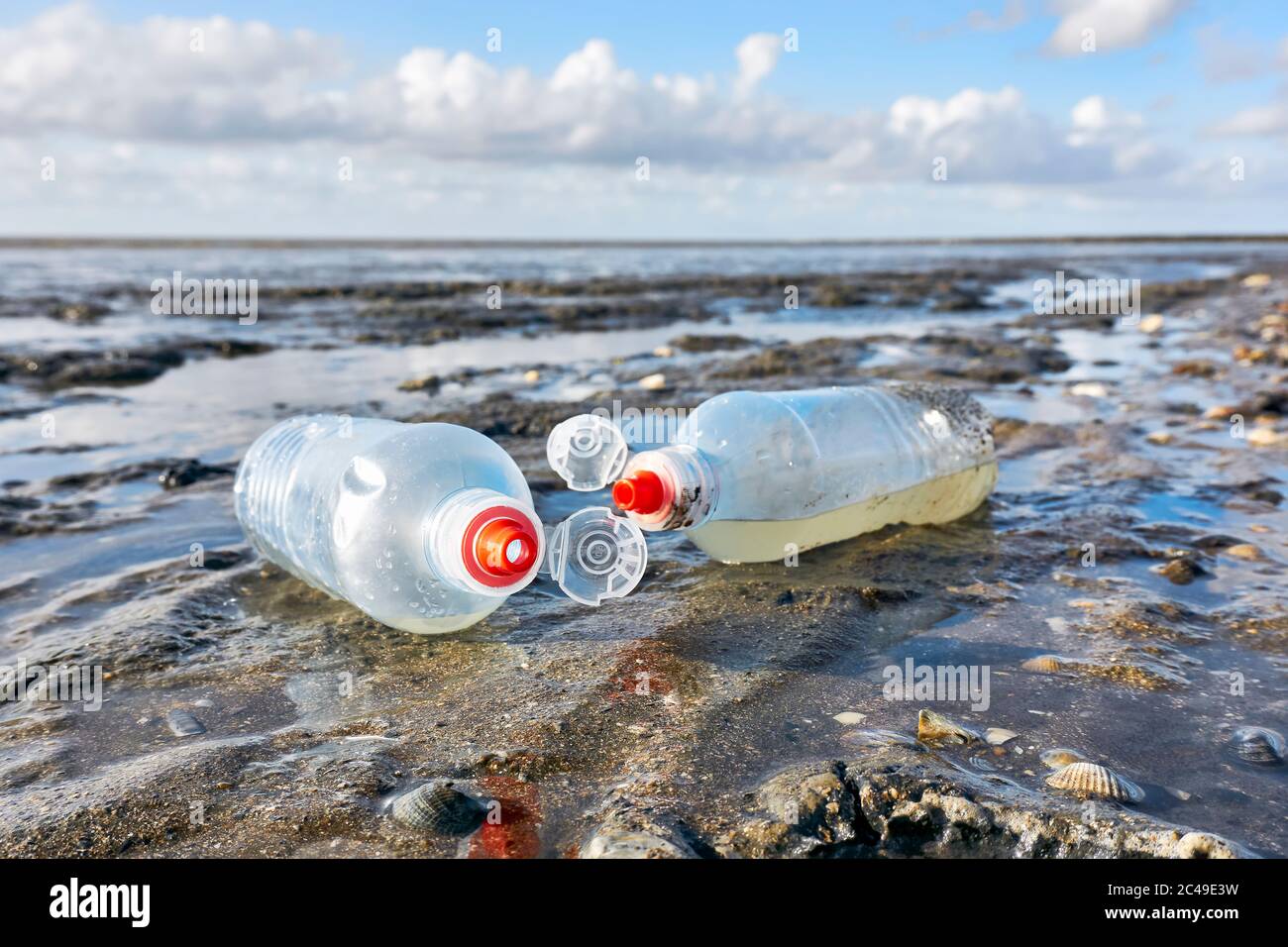 Plastic bottles with red bottle caps on a beach with blue sky at low ...