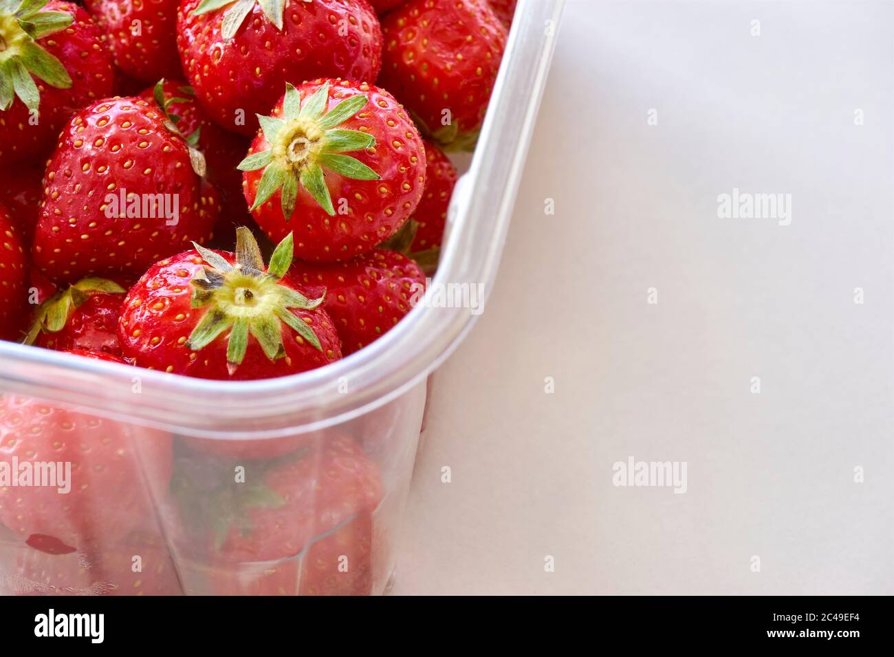 Fresh ripe strawberries in a clear plastic container on white background. Image with copy space ...