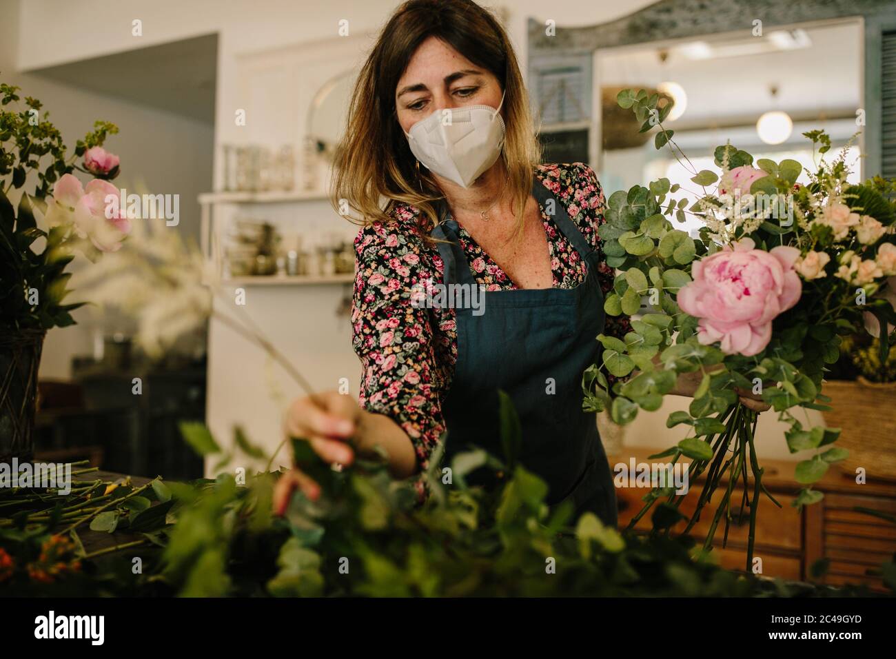 European female florist with a medical face mask making flower ...