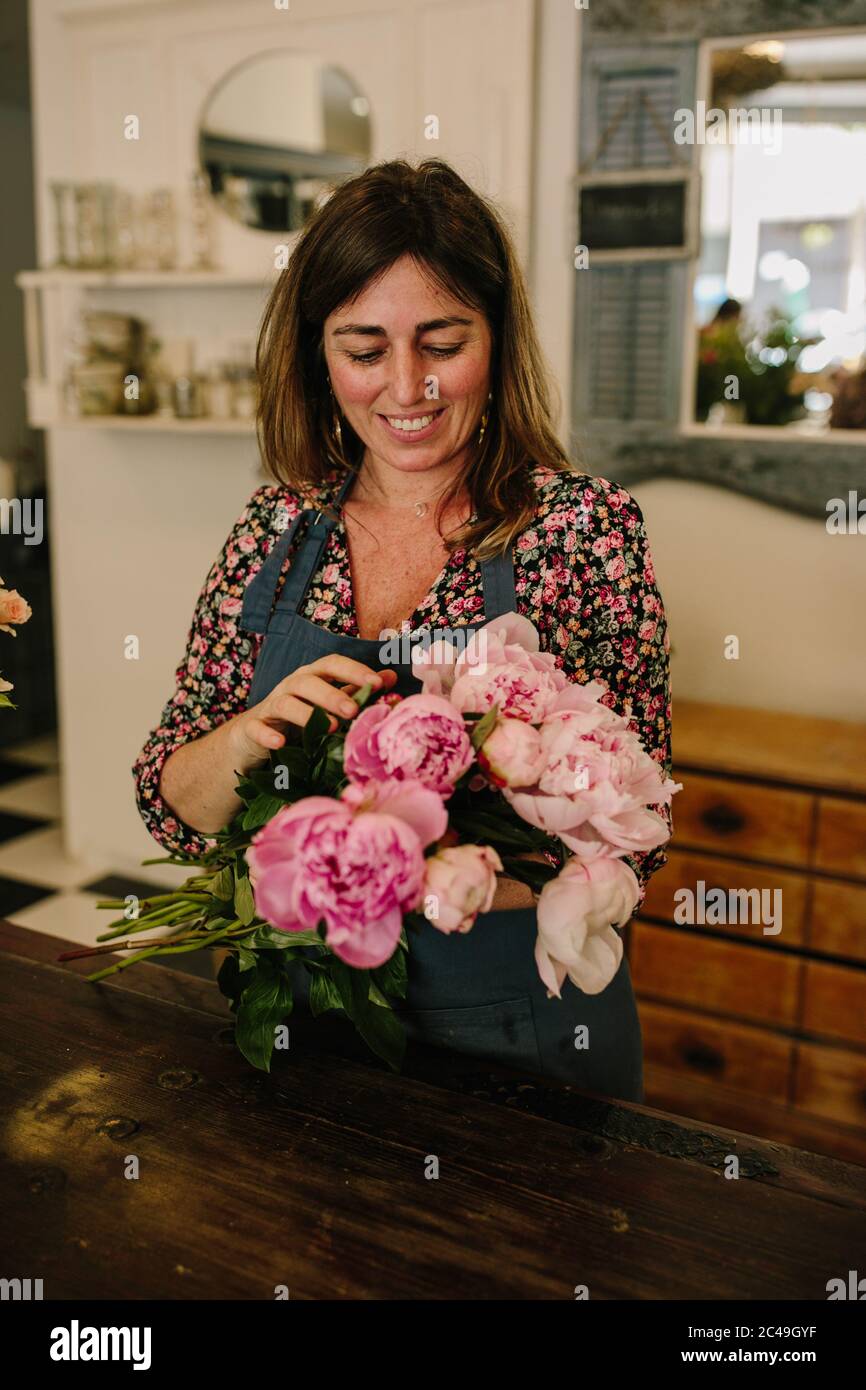 European female florist with a green apron making flower arrangements ...