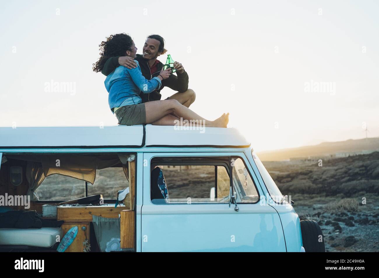 Happy couple cheering with beers on top of roof minivan - Travel couple ...