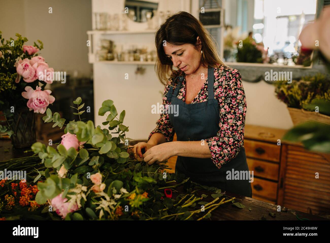 European female florist with a green apron making flower arrangements ...