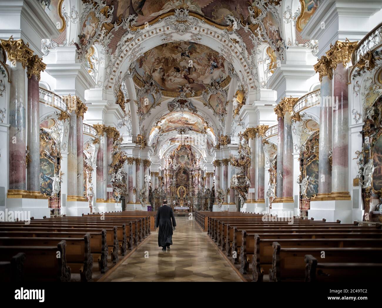 A priest walks to the altar of baroque monastery church Zwiefalten ...