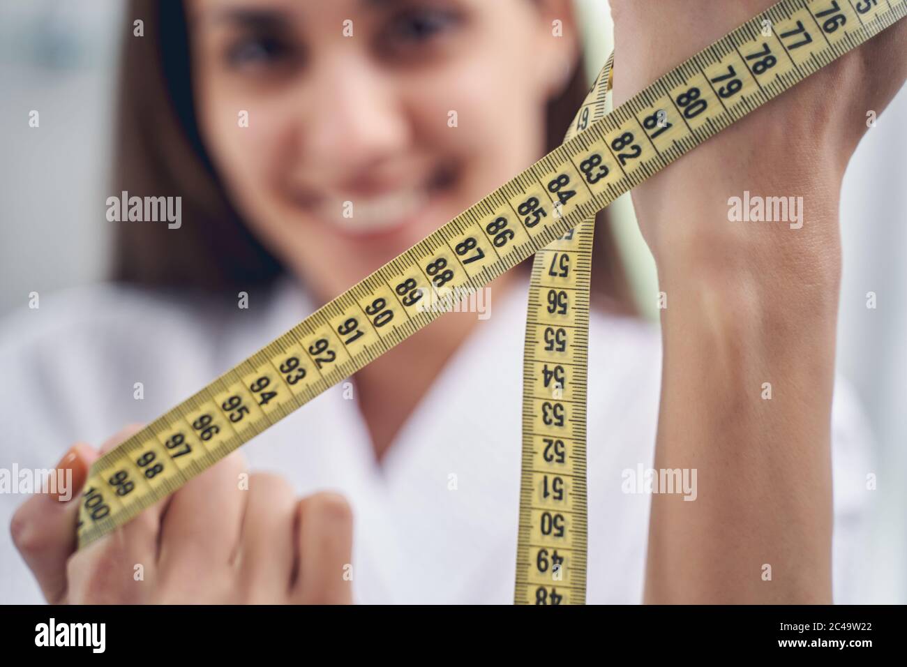 Smiling young woman holding yellow measuring tape Stock Photo - Alamy