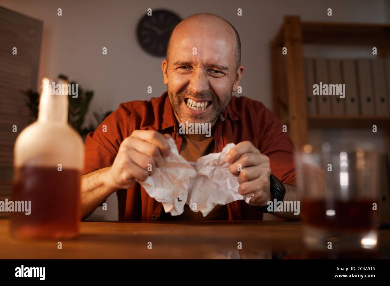 Portrait of mature angry man sitting at the table with bottle of wine ...