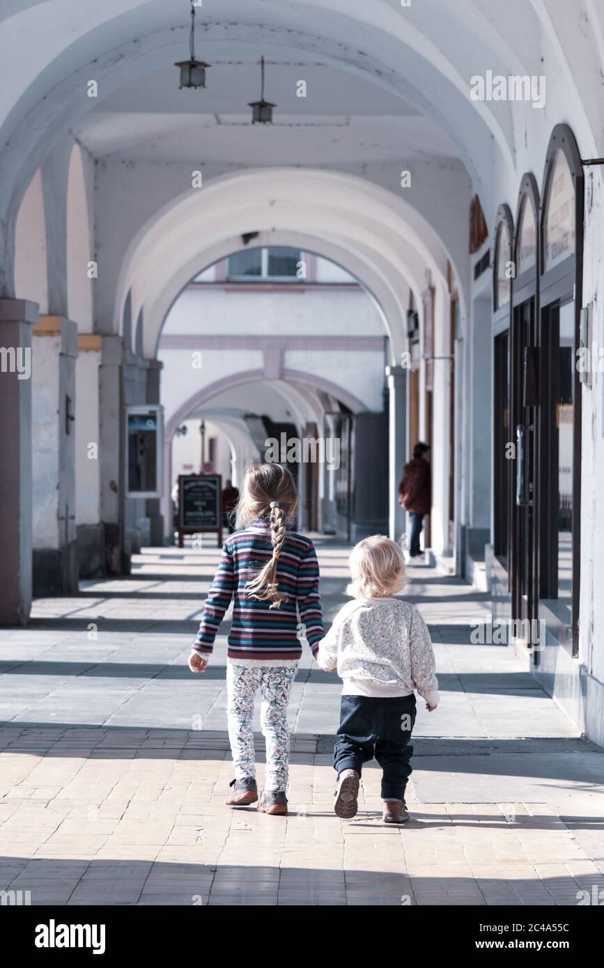 Two young children walk together hand in hand in the old town arcade ...