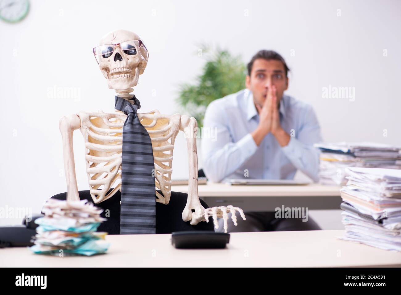 Young employee and skeleton in the office Stock Photo - Alamy