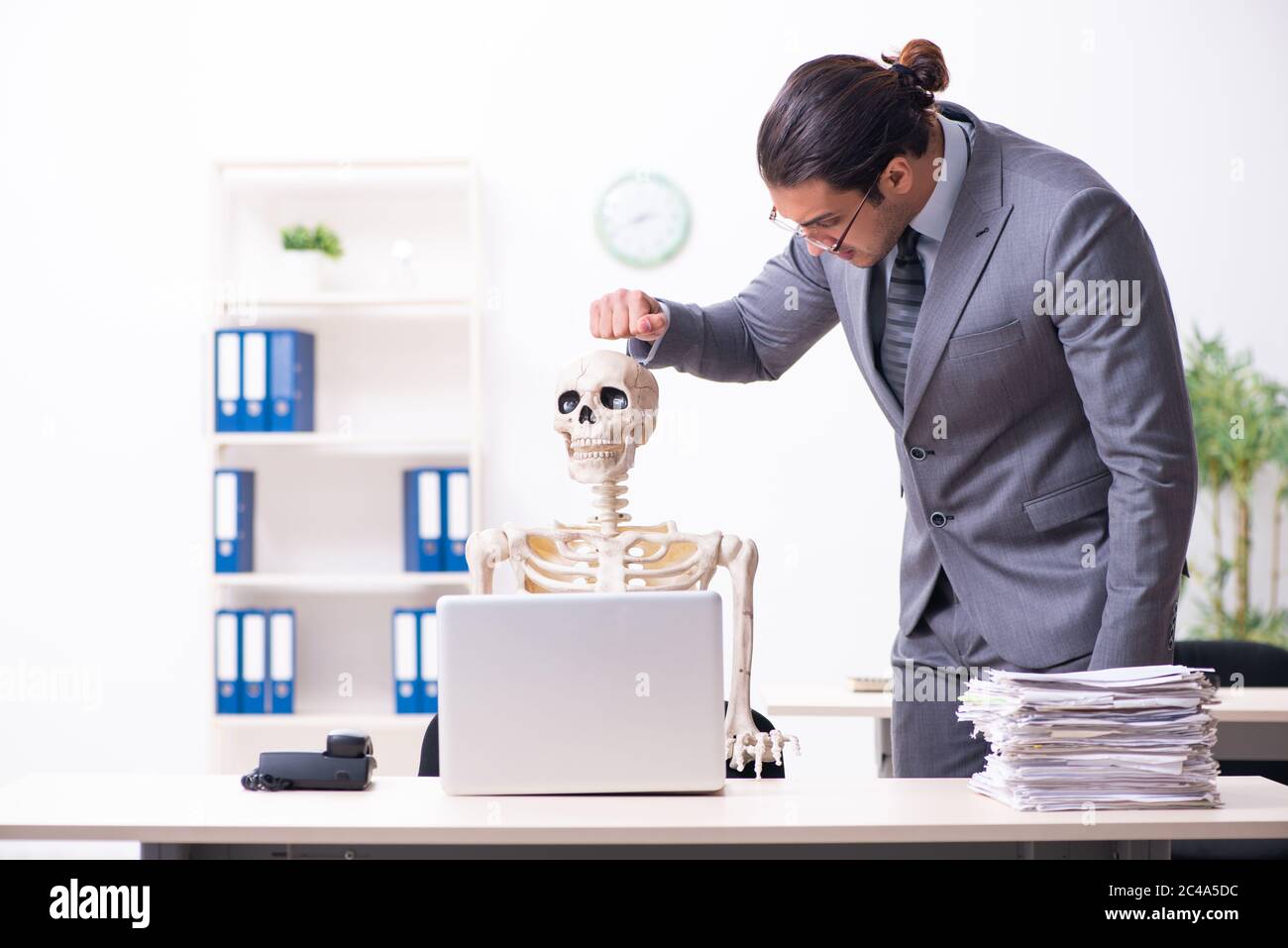 Young employee and skeleton in the office Stock Photo - Alamy