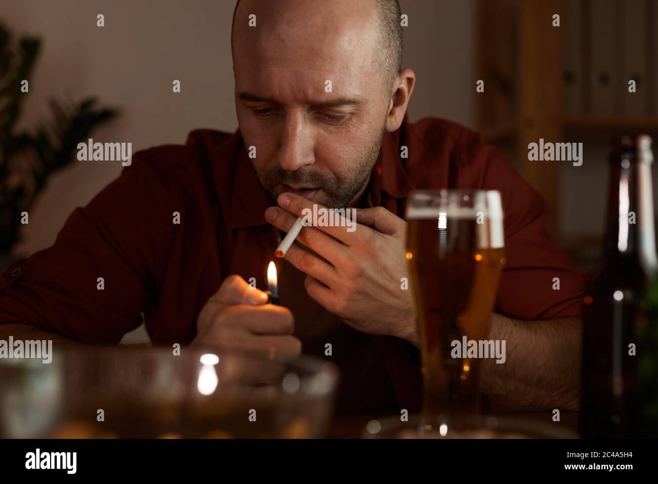 Mature man sitting at the table smoking cigarette and drinking beer ...