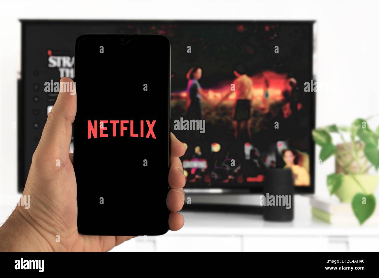 Hand holding a mobile with the Netflix app logo on it in a living room ...