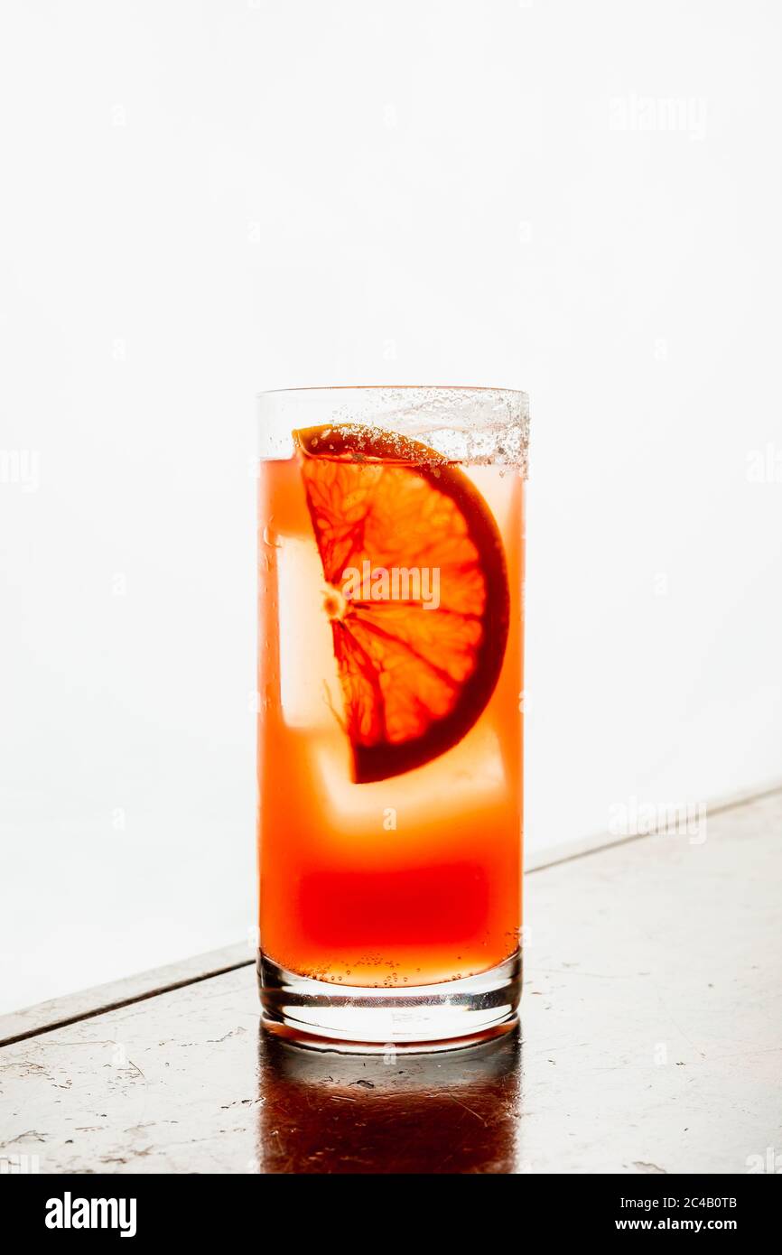 An orange cocktail in a highball glass filled with ice and garnished ...