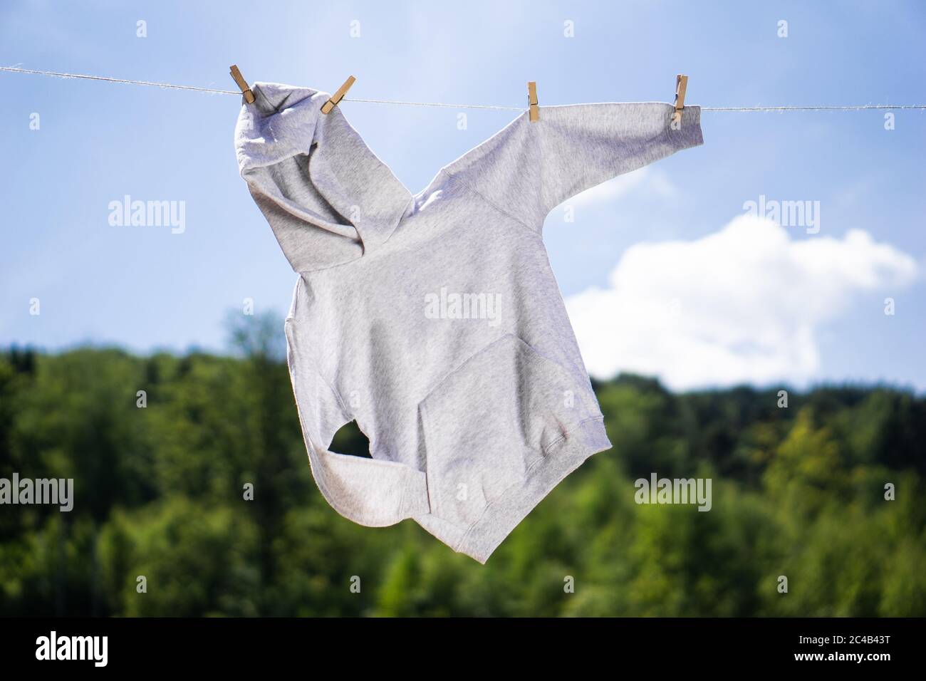 Gray hoodie mockup hanging on the rope with clothespins in front of ...