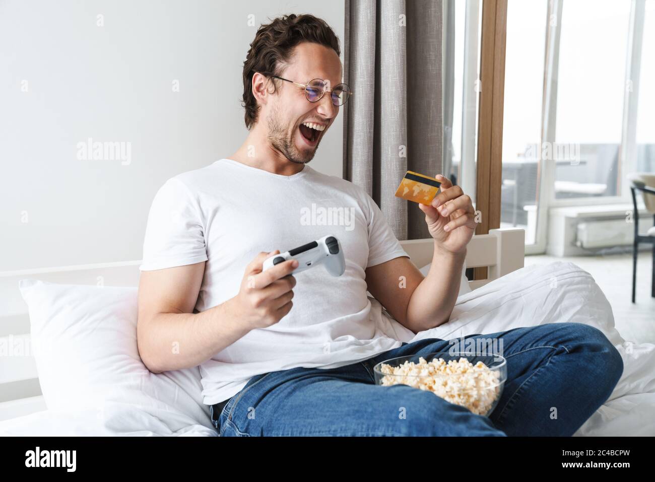 Handsome cheerful young man playing on playstation while laying on bed ...