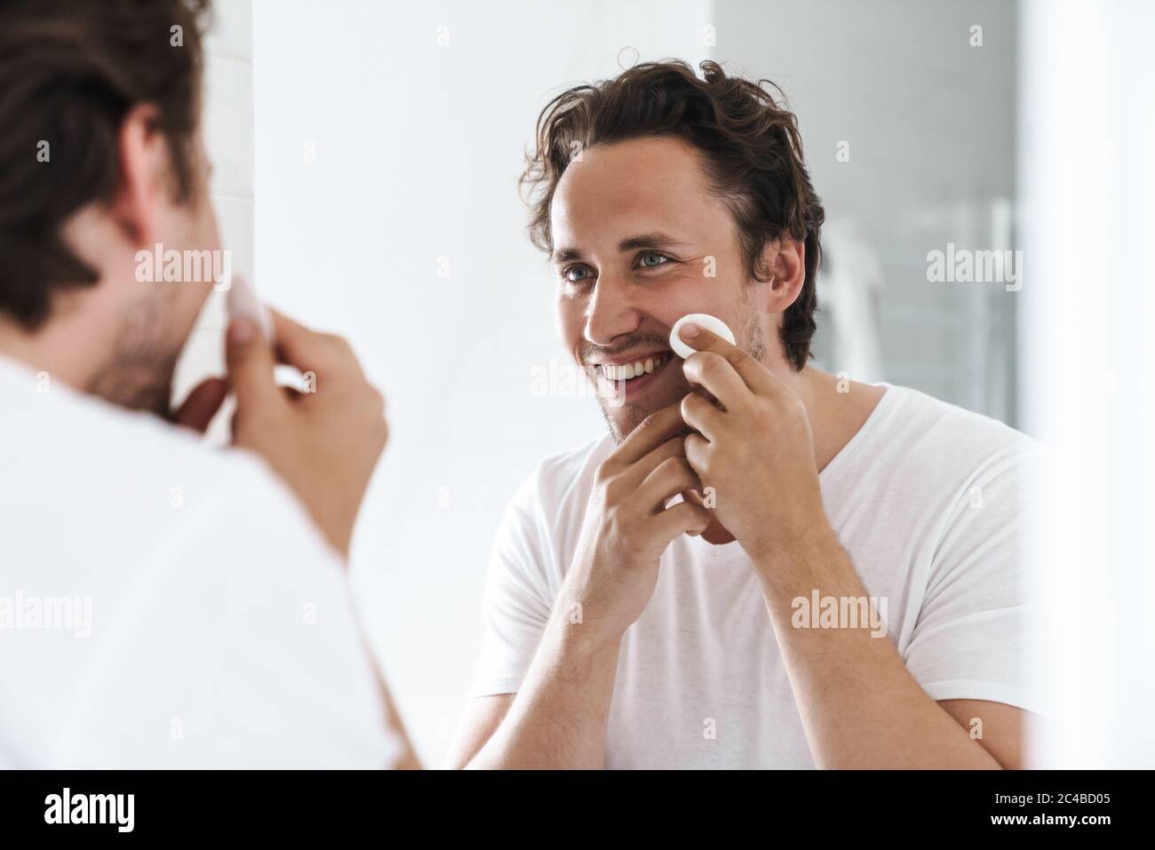 Attractive happy young man standing in front of the bathroom mirror ...