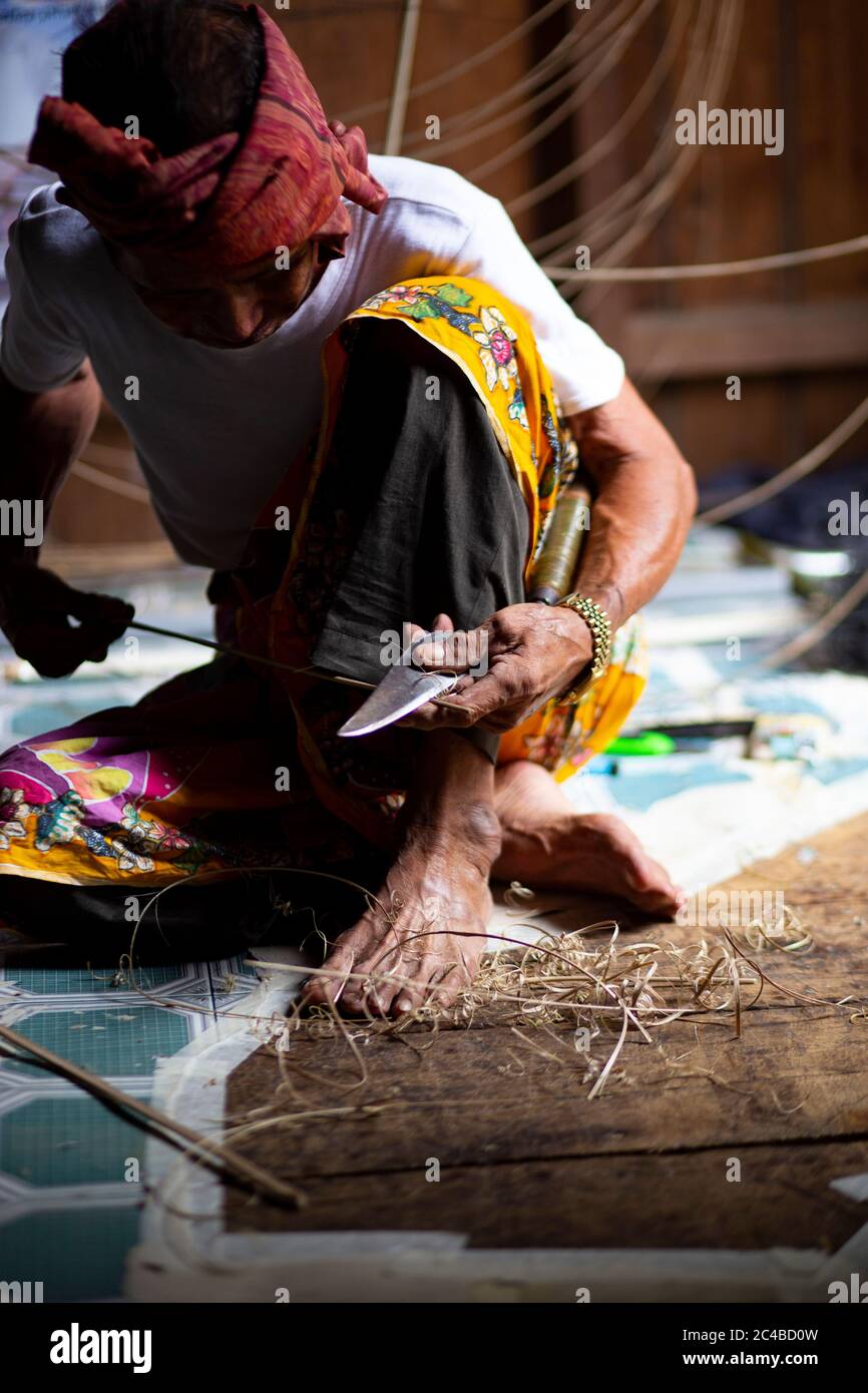 Malaysian kite maker working on a kite in his workshop in low light ...
