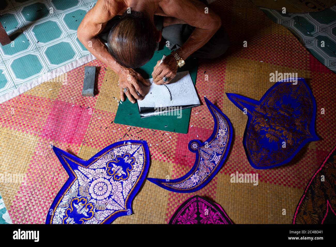 Malaysian kite maker working on a kite in his workshop in low light ...