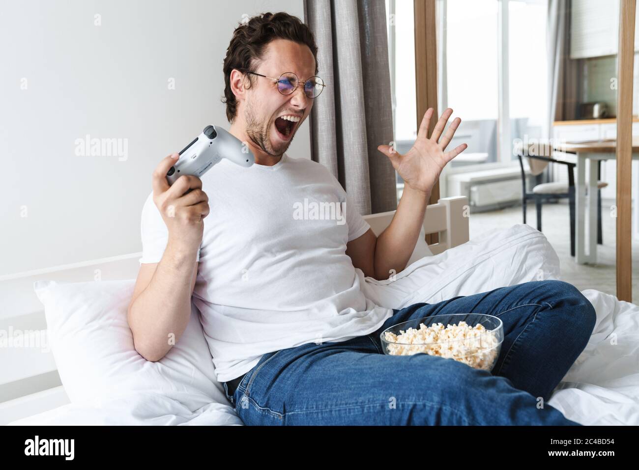 Handsome cheerful young man playing on playstation while laying on bed ...