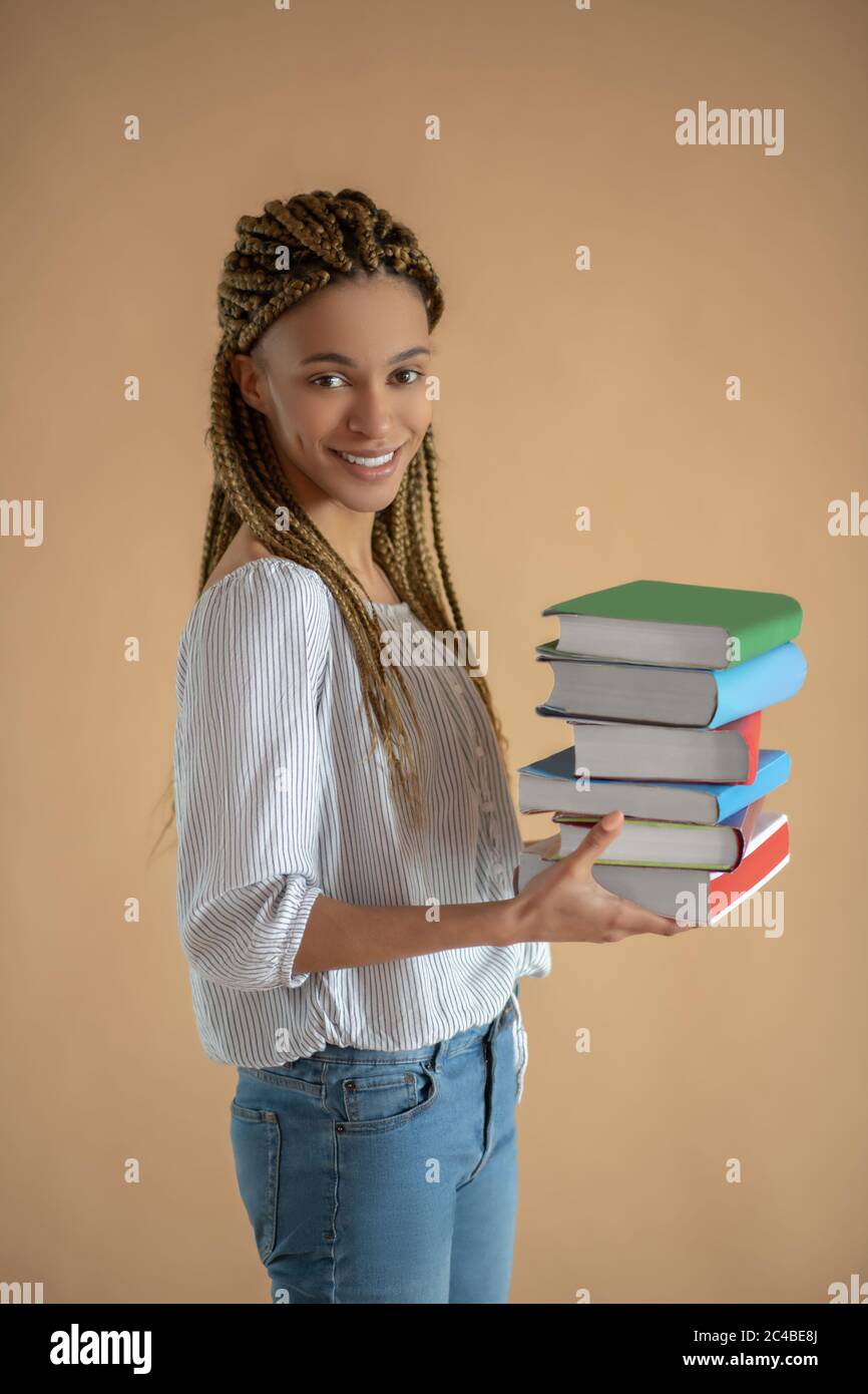 Happy young African American female carrying pile of books in front of ...