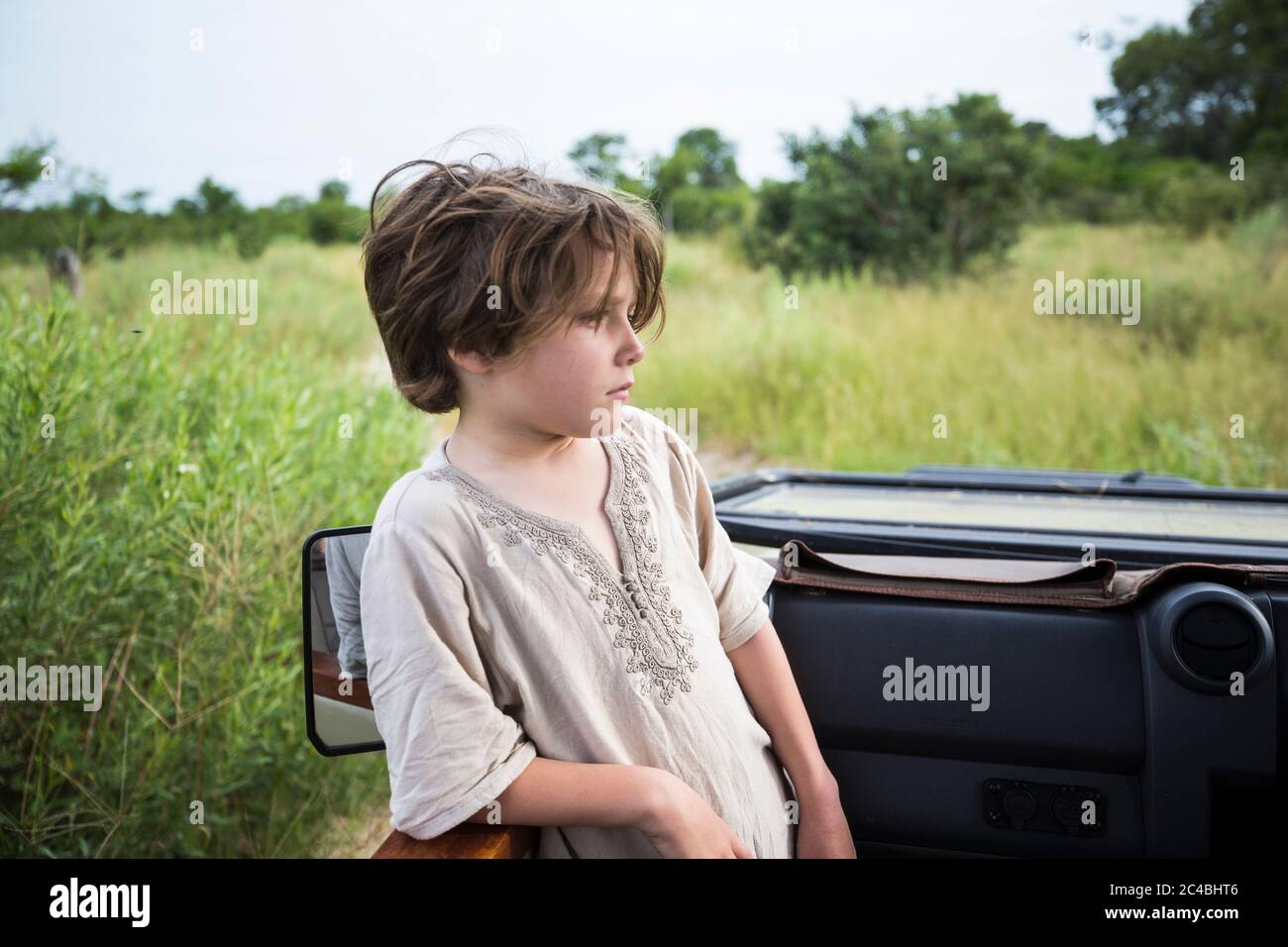 Six year old boy standing looking around the landscape in a safari jeep ...