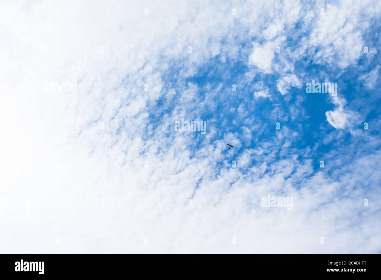 View up to opening of blue sky above white cloud cover, small aircraft ...