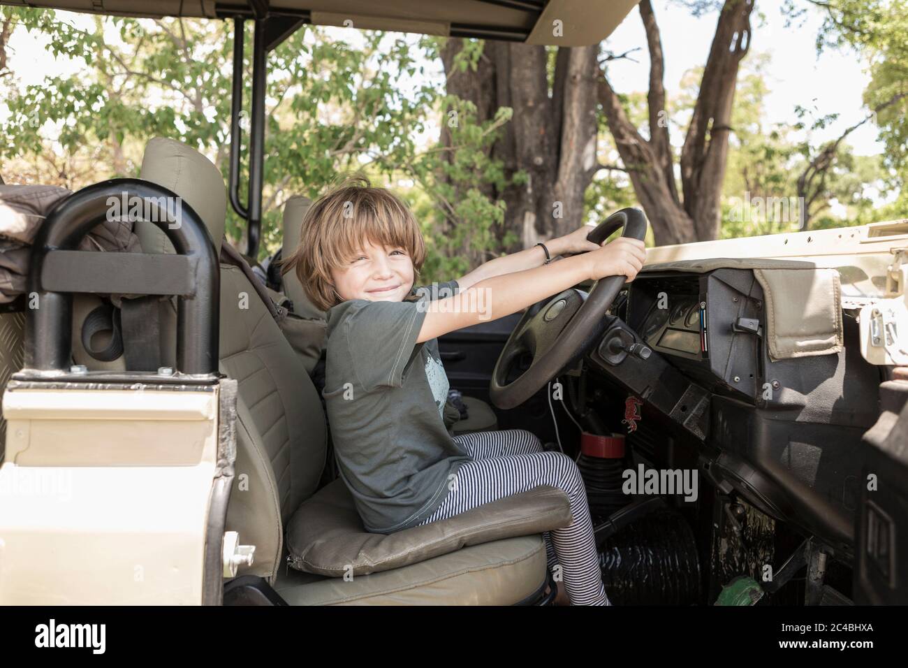 A five year old boy seated in the driving seat of a safari jeep ...